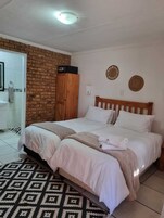 Uma cama de casal com cabeceira de madeira, parede de tijolos, um pequeno armário de madeira e um tapete estampado.
