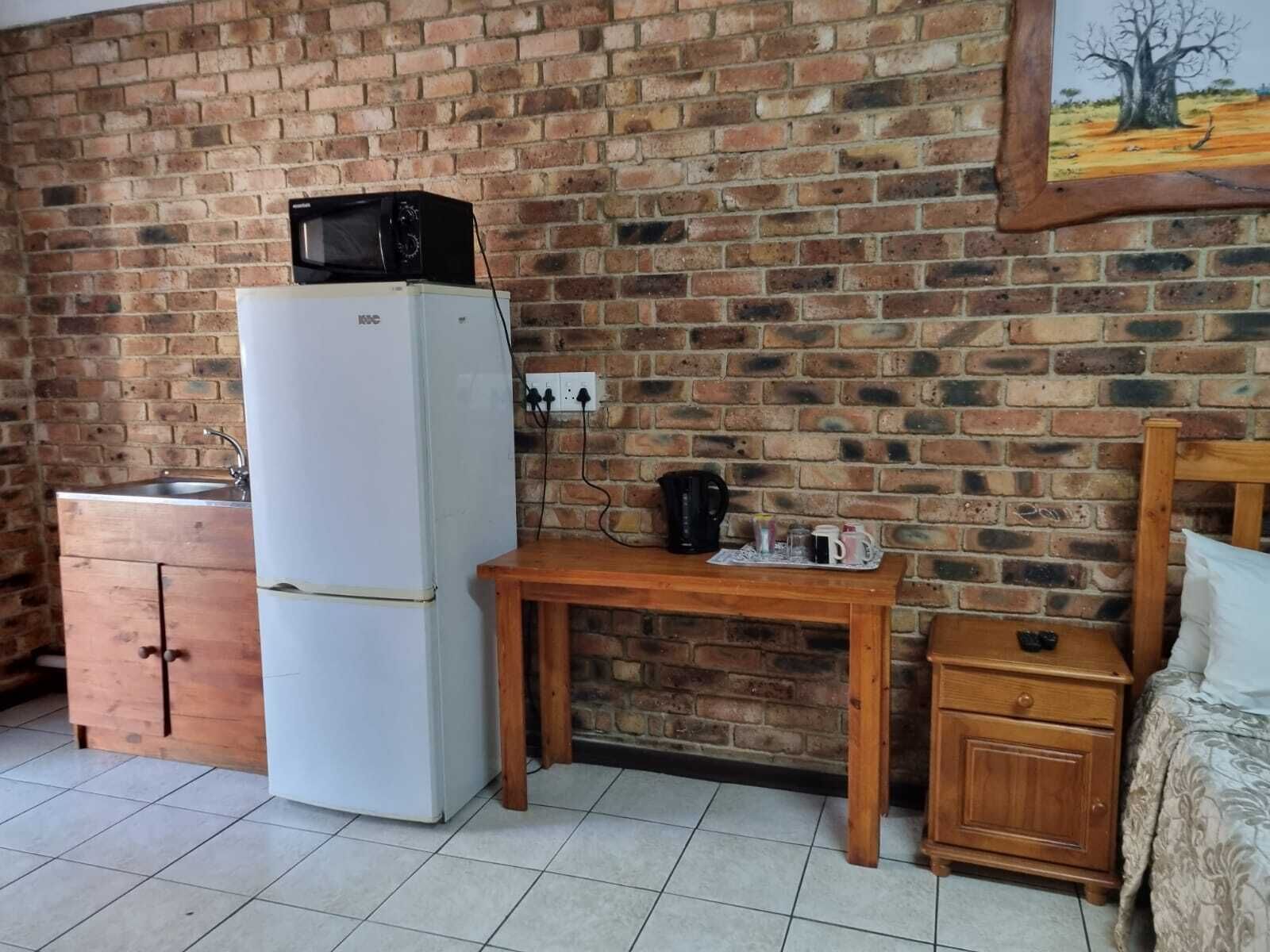 Cozinha compacta com geladeira, micro-ondas, pia, mesa de madeira e mesa de cabeceira com luminária.