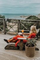 Uma pessoa relaxando em um deck de madeira com vista para o mar e uma linha de costa distante.
