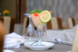 Um cocktail num copo de martini sobre uma mesa com um descanso, uma colher e um guardanapo.
