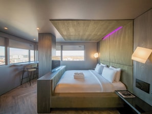 Quarto de hotel moderno com uma cama grande, uma mesa de escritório e vista para a cidade.