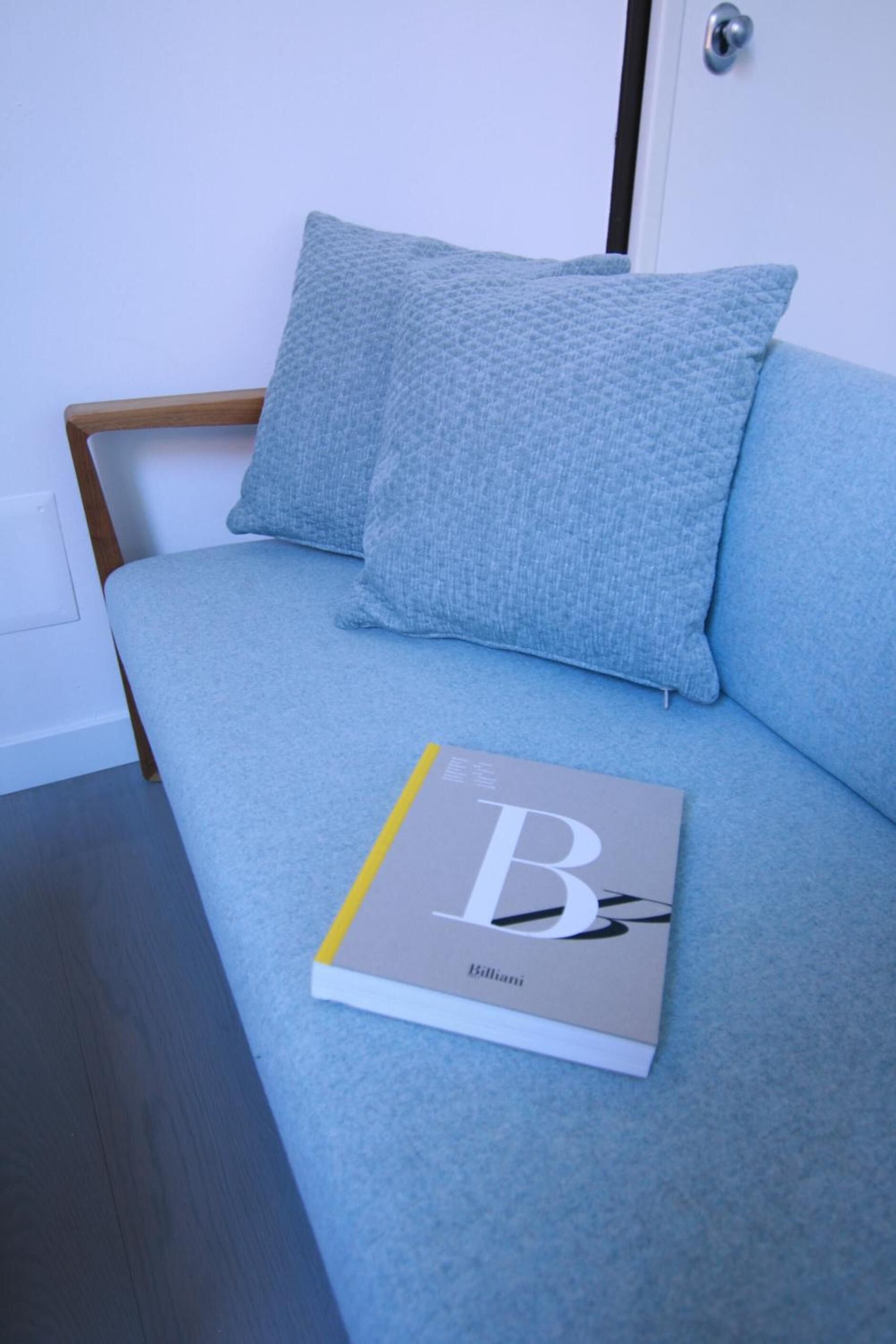 Um sofá azul claro com uma almofada e um livro intitulado 'B' de Billiardi.