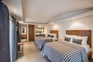 Quarto de hotel com duas camas, um espaço para sentar pequeno e um banheiro visível através de uma porta aberta.
