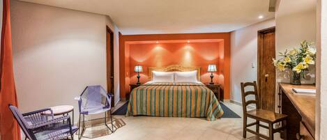 Quarto de hotel com cama, duas cadeiras, escrivaninha e mesa de cabeceira.