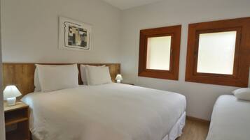 Quarto de hotel com uma cama grande, duas mesas de cabeceira com abajures e duas janelas com molduras de madeira.