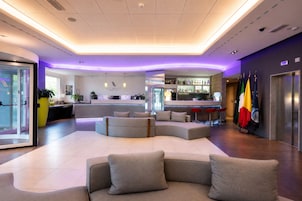 Um hall de hotel com balcão de recepção, área de estar, bar e bandeiras.