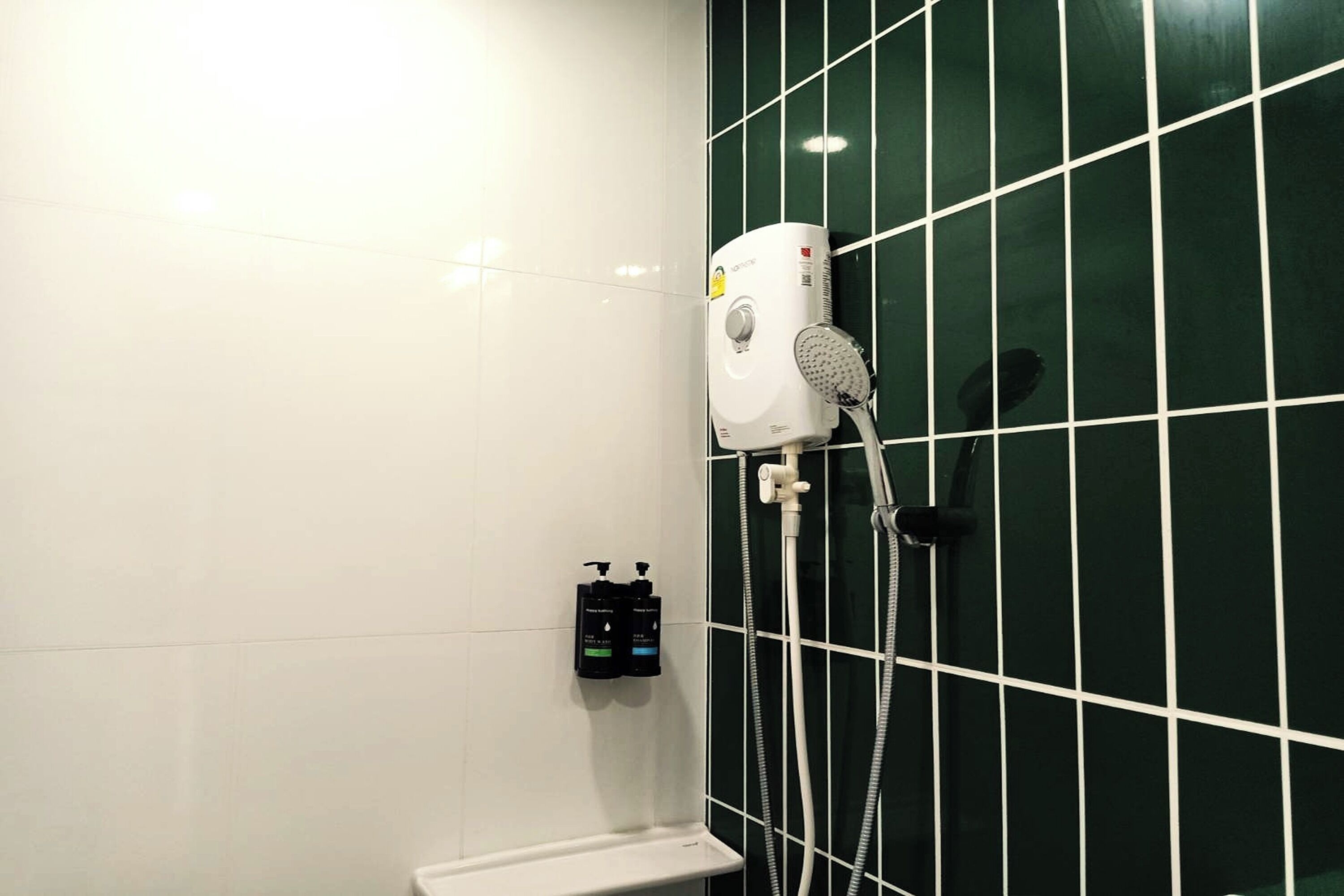 Área de chuveiro com chuveiro manual, painel de controle na parede e uma pequena prateleira.
