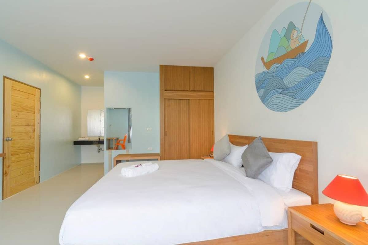Quarto com cama grande, guarda-roupa de madeira, banheiro com espelho e parede com pintura de barco.
