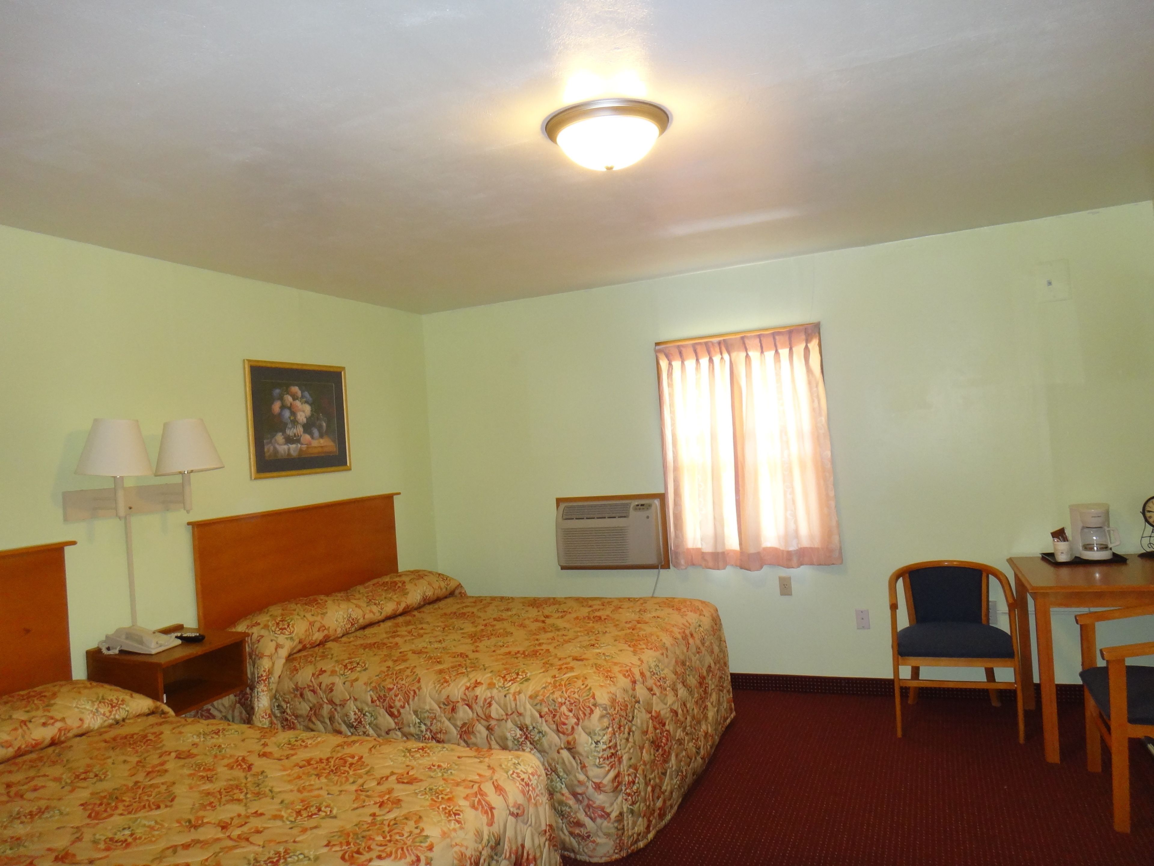 Quarto de hotel com duas camas, uma escrivaninha, uma cadeira, uma luminária, um quadro na parede e um aparelho de ar condicionado.