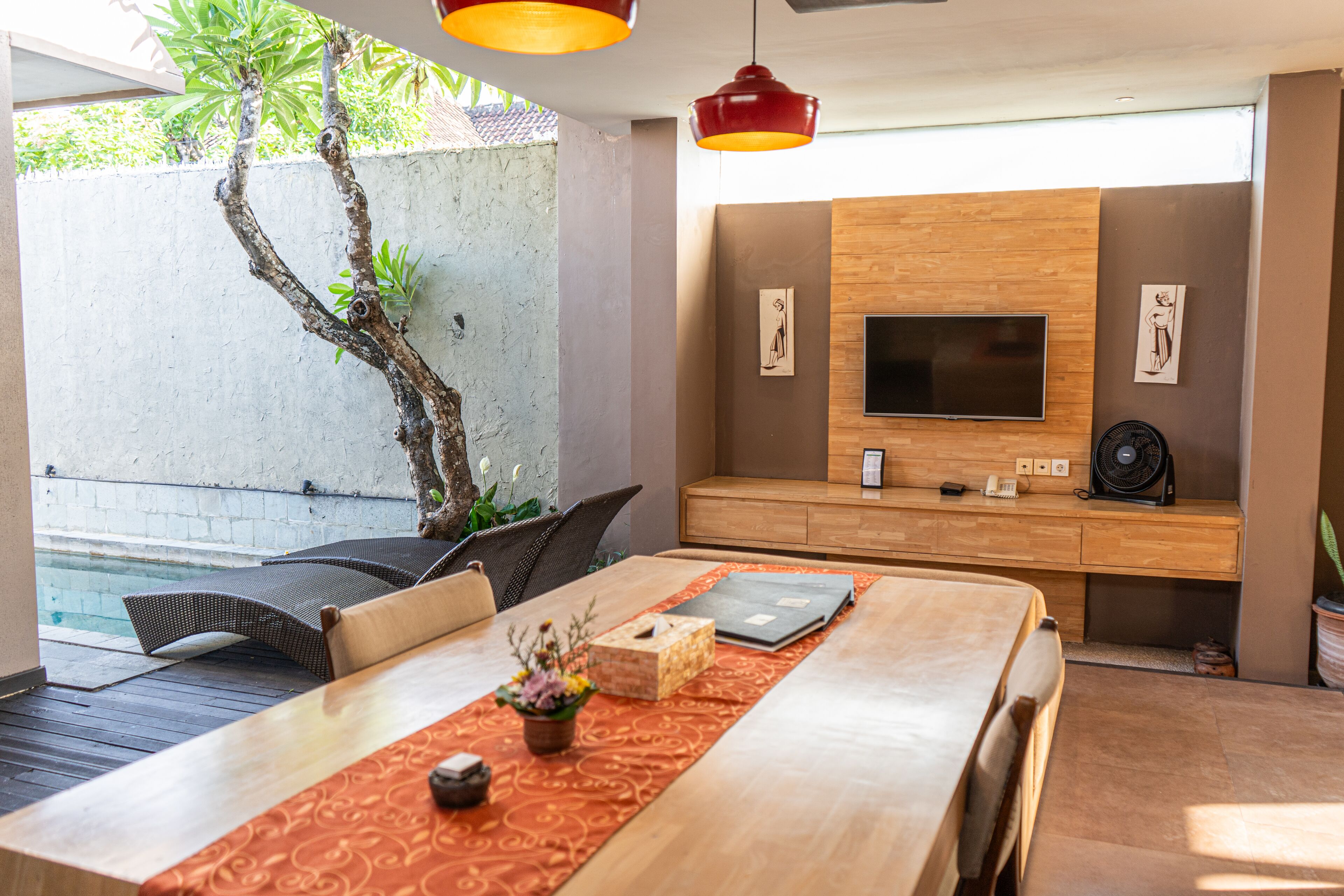 Uma área de refeições moderna com mesa de madeira, cadeiras, um tapete vermelho e uma TV fixada numa parede de madeira.
