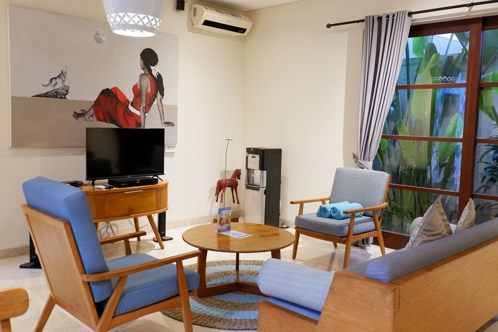 Sala de estar com televisão, móveis de madeira, escultura de cavalo e vista para o verde pela janela.