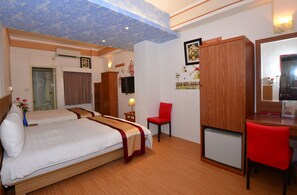 Quarto de hotel com duas camas, uma escrivaninha, uma cadeira, um refrigerador e uma televisão.