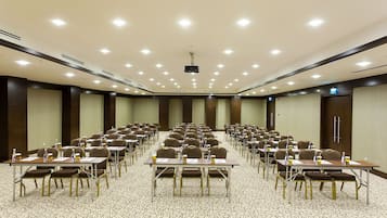 Uma sala de conferências com mesas e cadeiras dispostas em fileiras, equipada com garrafas de água e blocos de anotações.