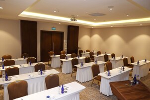 Sala de conferências com várias mesas e cadeiras, equipada com garrafas de água e placas de identificação.