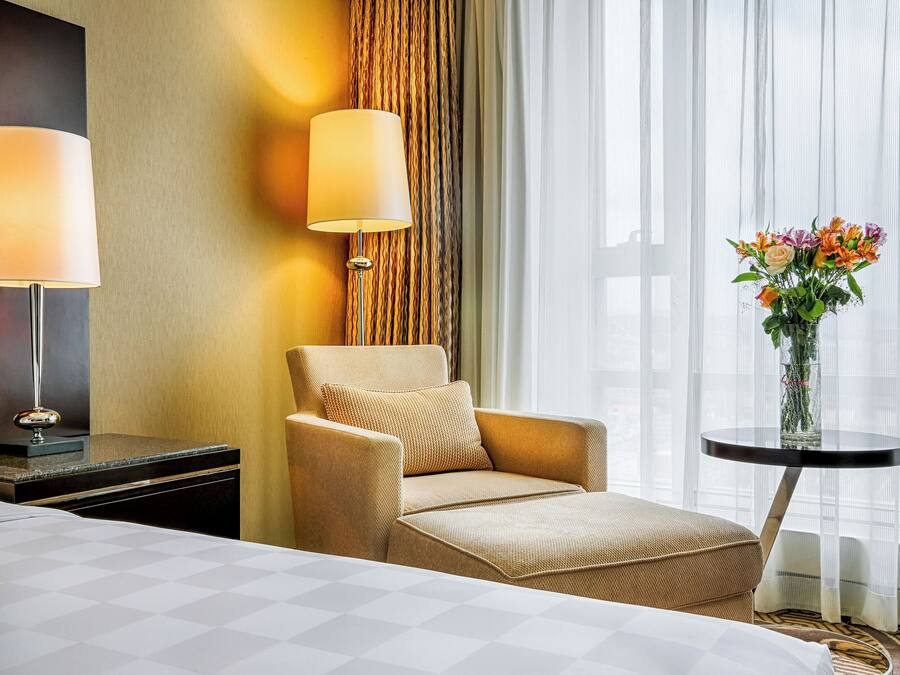 Quarto de hotel com cama, sofá, mesinha com um vaso de flores e duas luminárias.