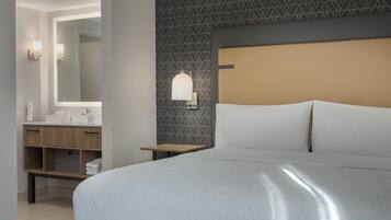Quarto de hotel com uma cama grande, uma mesa de cabeceira de madeira, um espelho, uma luminária fixada na parede e um papel de parede estampado.