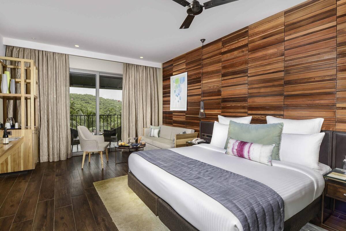 Quarto de hotel moderno com uma cama grande, painéis de madeira nas paredes, uma varanda com vista e uma escrivaninha com cadeira.