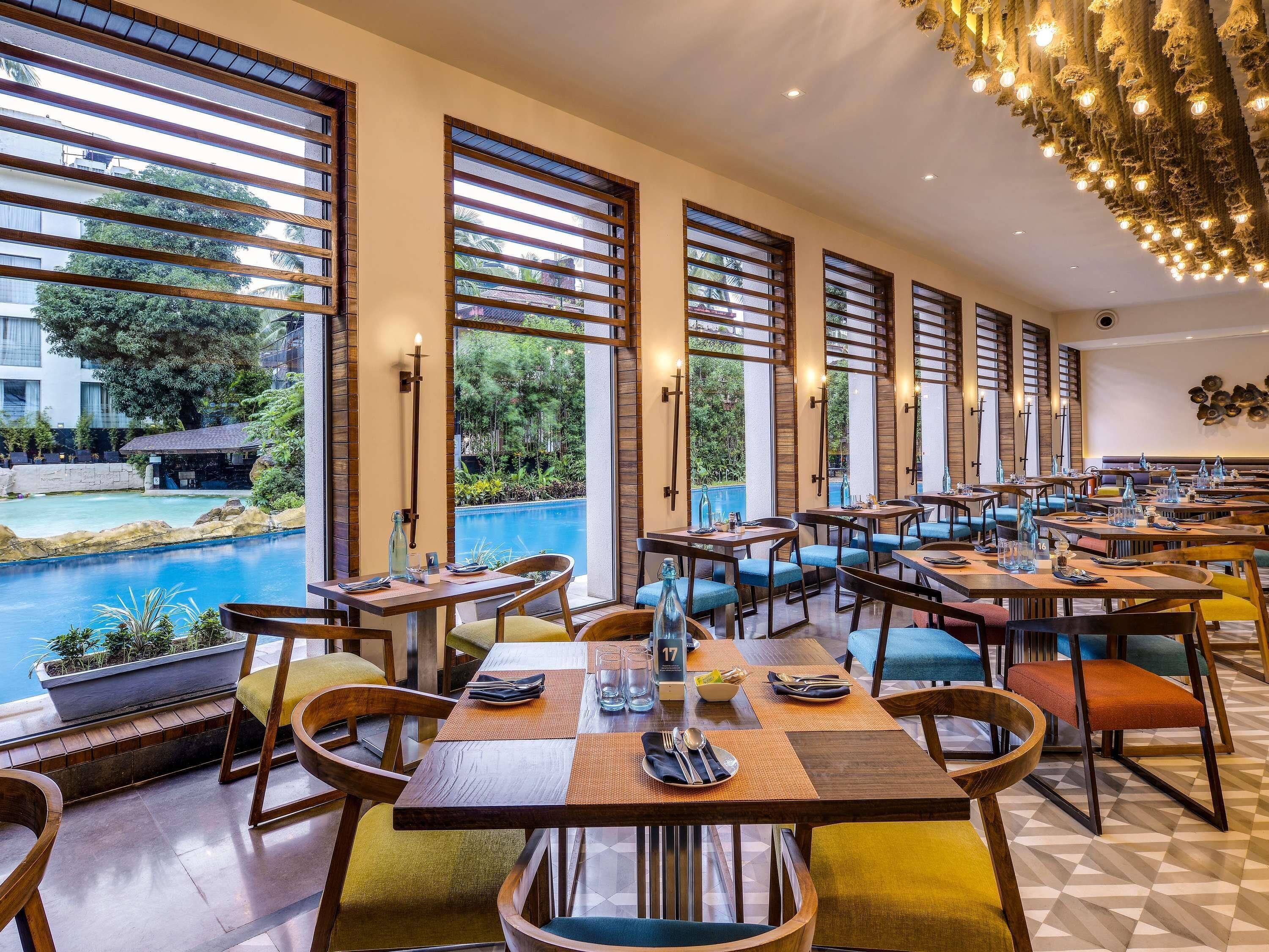 Um restaurante com mesas ao ar livre, janelas amplas e vista para a piscina.