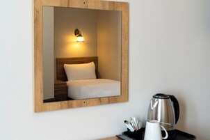 Quarto de hotel com cabeceira de madeira, luminária de cabeceira, cama, mesa de cabeceira, cafeteira e xícara de café em um suporte.