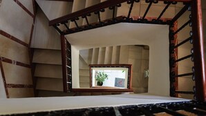 Escada de madeira com corrimão e um pequeno espelho refletindo um quarto com uma planta e um quadro emoldurado.