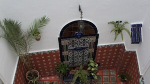 Terraço no telhado com piso de azulejos, mesa de madeira e vários vasos de plantas.