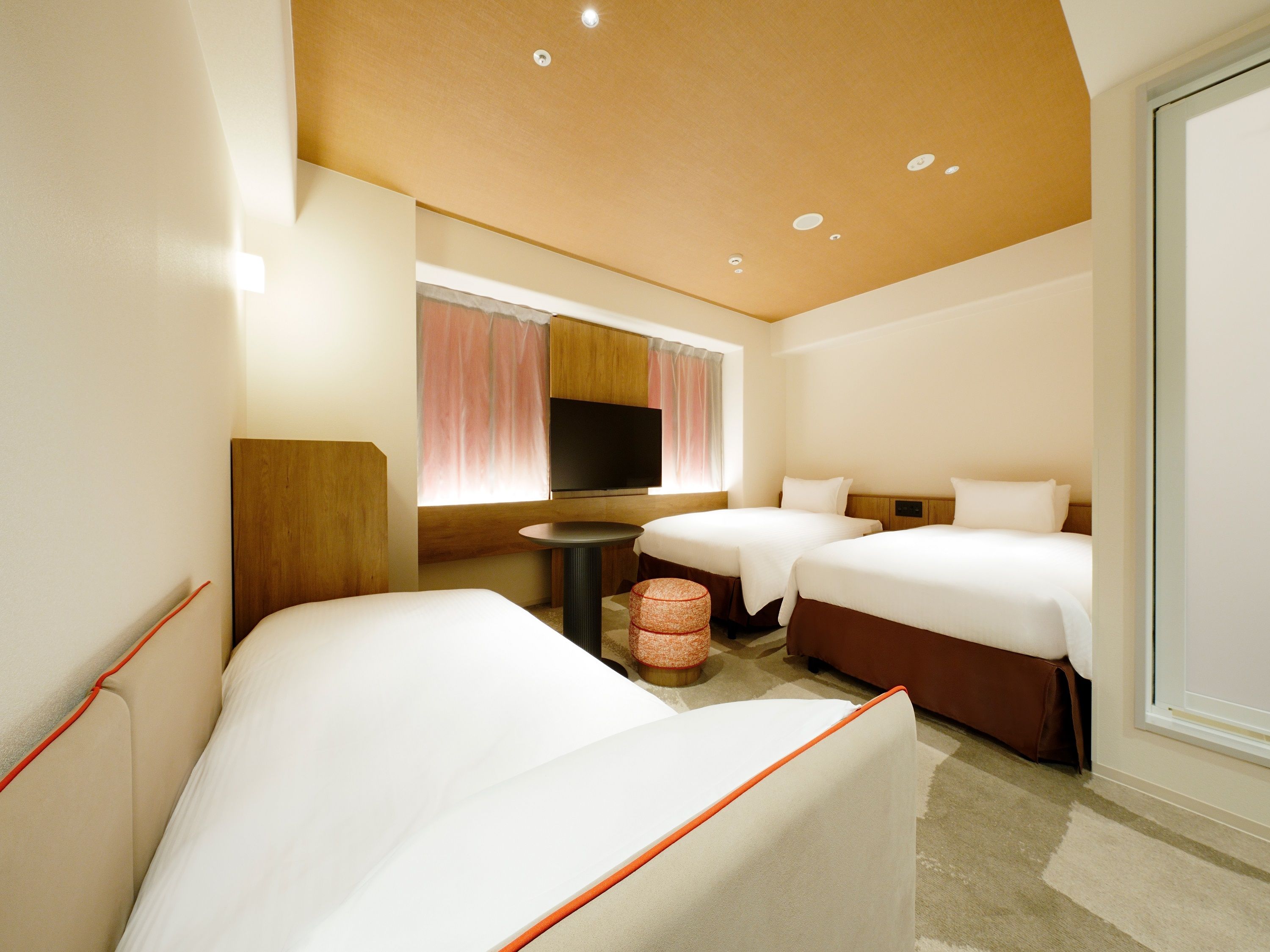 Quarto de hotel com duas camas, uma mesa redonda pequena, televisão e janela com cortinas.