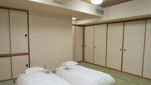 Quarto japonês tradicional com tatames, duas camas de solteiro com roupa de cama branca e uma mesa de madeira baixa com um tabuleiro de artigos de higiene.