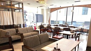 Interior de restaurante com disposição de mesas, um canto para café e grandes janelas.