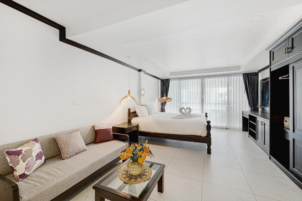Quarto de hotel moderno com cama, sofá, mesa de centro com flores e televisão.