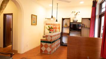 Uma área de recepção com piso em azulejos, balcão de atendimento, ventilador de teto, luminárias pendentes, estante e uma porta.