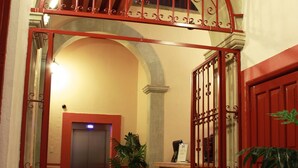Um corredor com um portão de ferro vermelho, um elevador e um vaso de plantas.