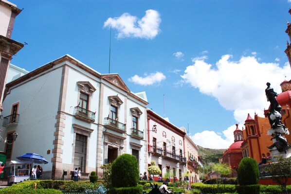 Um edifício histórico com arquitetura clássica, um jardim bem cuidado e uma estátua.