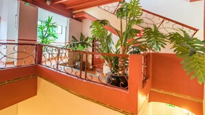 Varanda com grades de ferro forjado, plantas em vasos e vista do espaço interno.