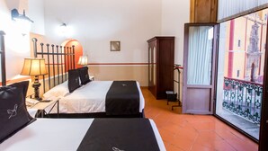 Quarto de hotel com duas camas, uma mesa de cabeceira, luminária, guarda-roupa e varanda com vista para edifícios.