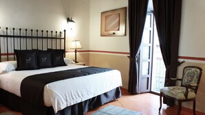Quarto de hotel com cama, poltrona, luminária, tapete e janela com cortinas.
