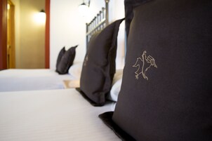 Quarto de hotel com duas camas, cada uma com almofadas escuras e desenhos bordados.