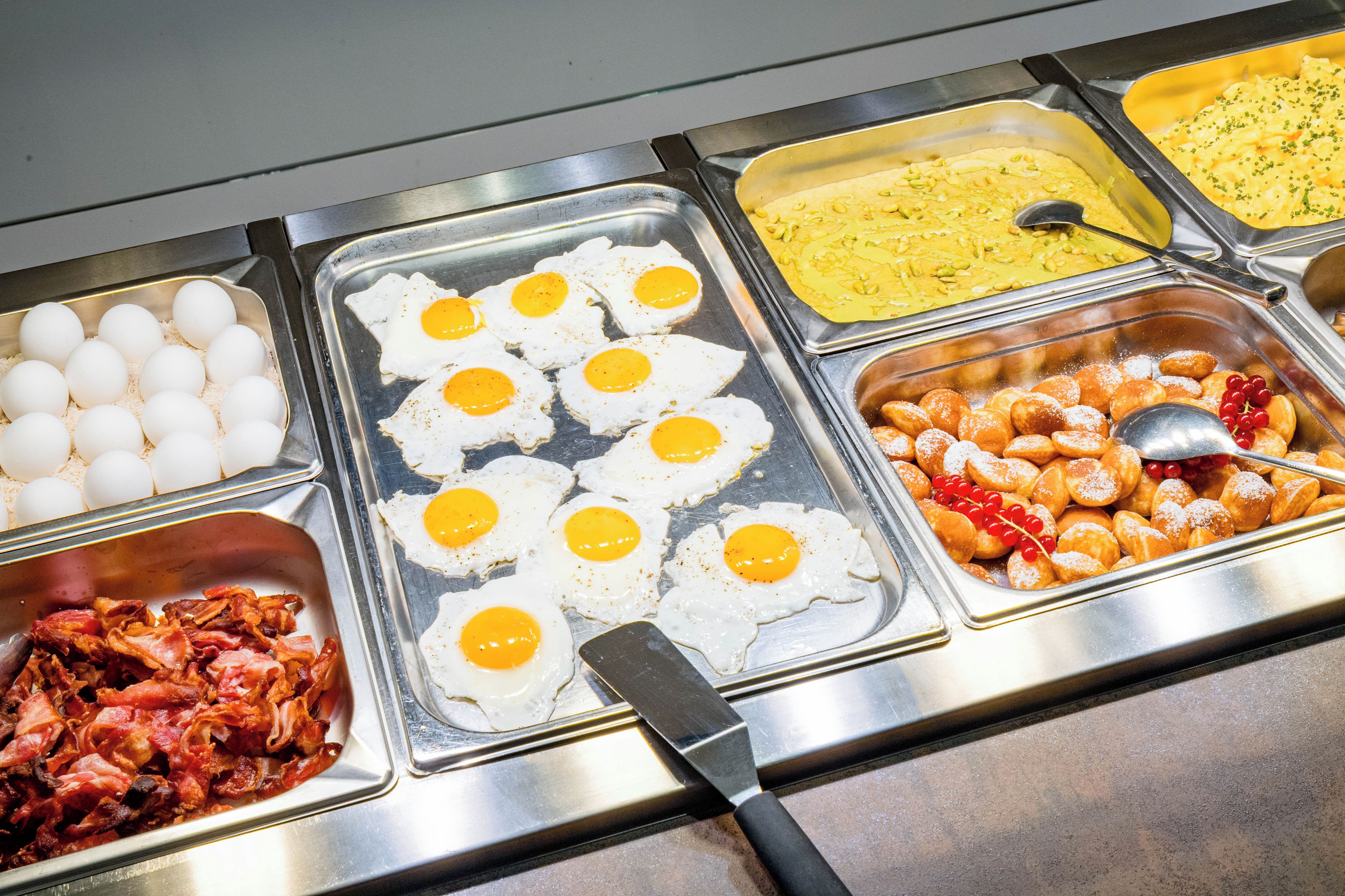 Buffet com diversas opções de comida, incluindo ovos, bacon e pães de confeito.