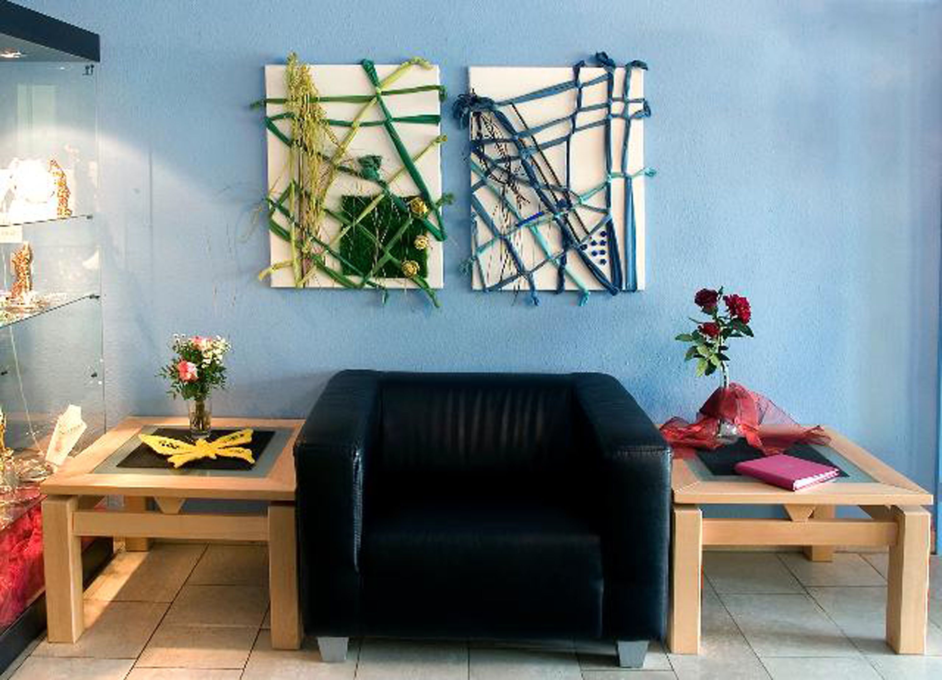 Sala de estar com sofá preto, duas mesas de madeira e duas obras de arte abstratas nas paredes.