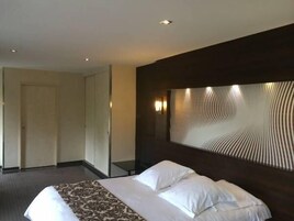 Quarto de hotel com uma cama grande, cabeceira escura e manta estampada.