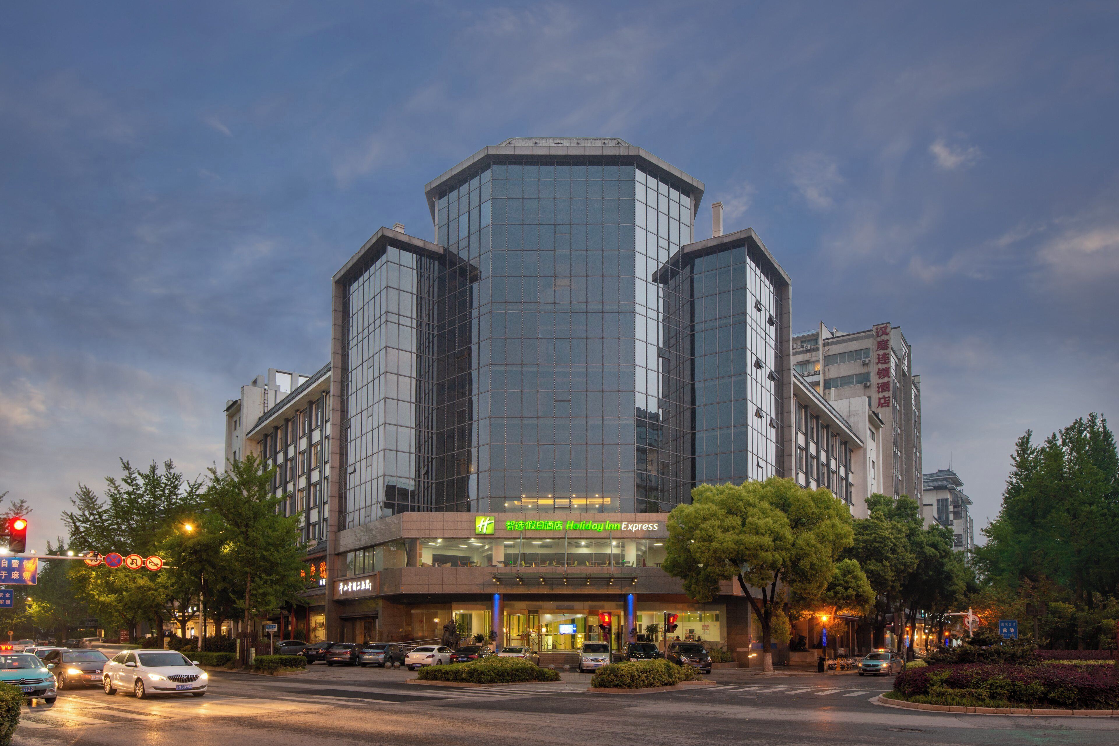 Um hotel moderno com fachada de vidro marcante e um elemento arquitetônico tradicional na lateral.