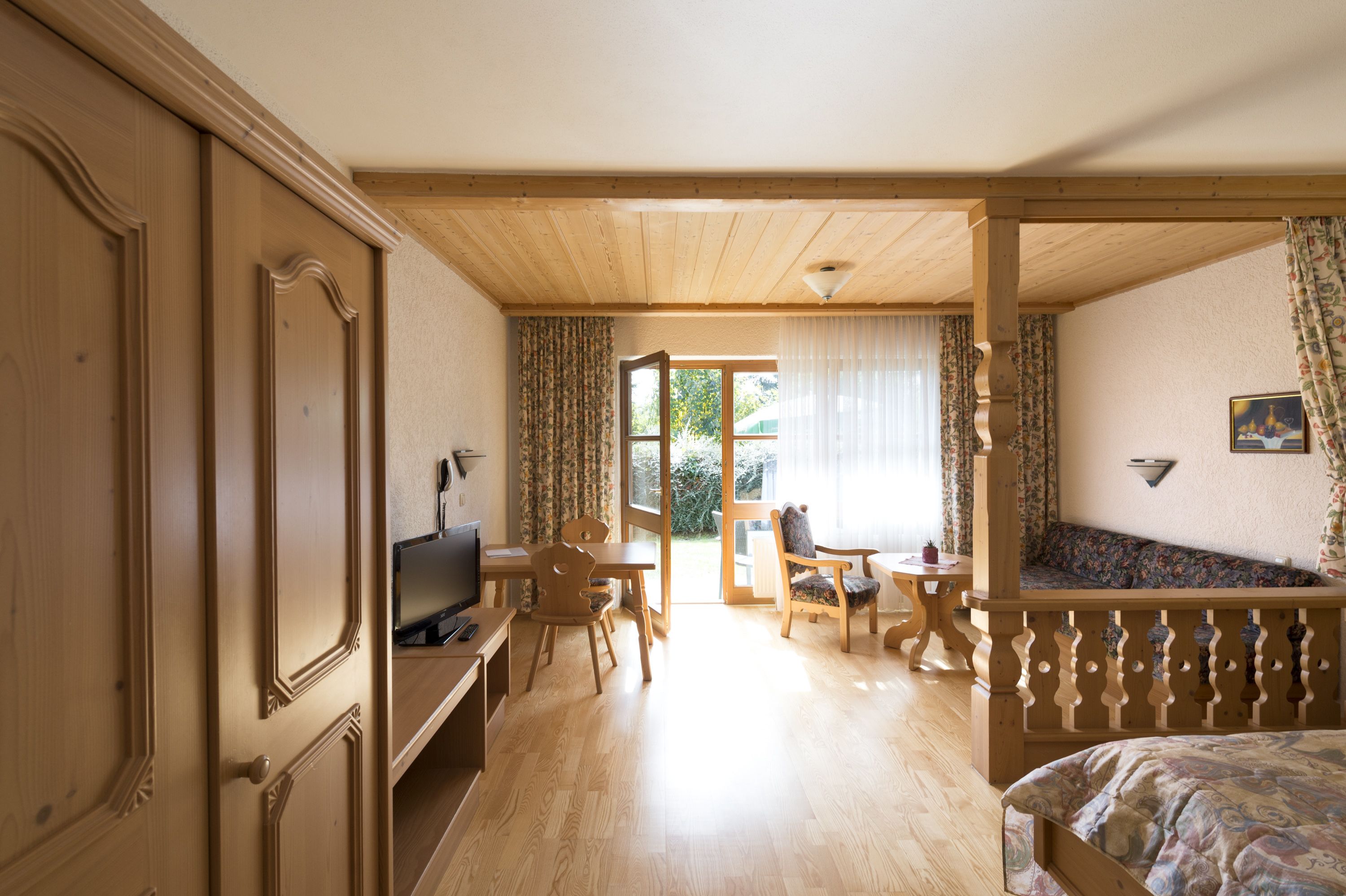 Quarto com escrivaninha de madeira, televisão, cama e varanda com guarda-corpo.