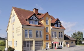 Um edifício grande de dois andares com várias portas de garagem, telhado vermelho e uma placa com a inscrição "Landgemäzgerei".
