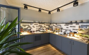 Cozinha moderna com armários cinza, painel de azulejos e diversos itens de café da manhã sobre o balcão.