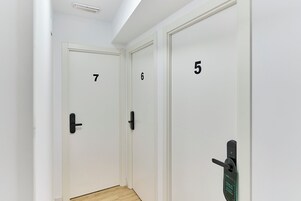 Um corredor com três portas numeradas 5, 6 e 7, cada uma com uma maçaneta moderna.