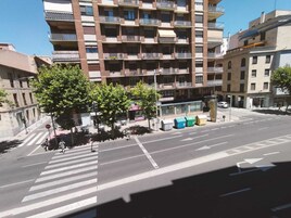 Um edifício residencial de vários andares com varandas, uma faixa de pedestres e uma rua com carros estacionados.