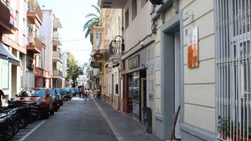 Rua estreita flanqueada por carros estacionados e edifícios com varandas.