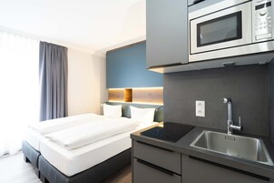 Quarto de hotel com cama, micro-ondas integrado, pia e mesa de cabeceira.
