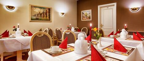Uma sala de jantar com mesas postas para refeição, com guardanapos vermelhos, toalhas de mesa brancas e velas.