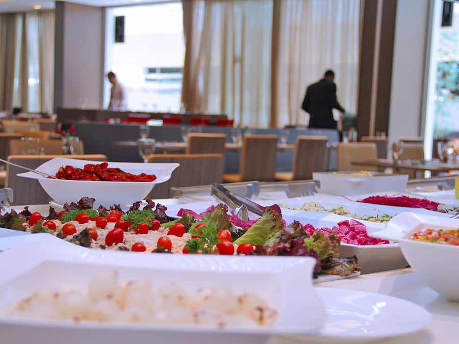 Buffet com diversos pratos e uma pessoa ao fundo.
