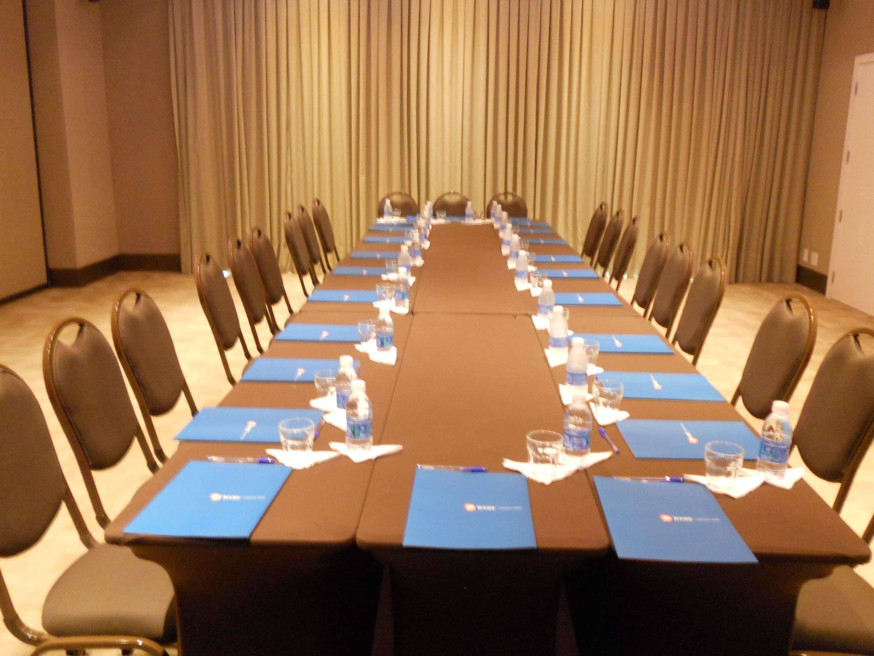 Uma sala de conferência com uma mesa comprida, cadeiras, garrafas de água e placas de identificação.